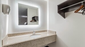 Uma casa de banho com lavatório de bancada em granito, espelho, porta-toalhas e dispensador de toalhas fixado na parede.