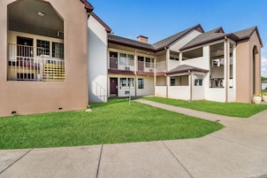 Um edifício residencial com vários andares, varanda coberta e gramado bem cuidado.