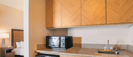 Uma cozinha compacta com armários de madeira, micro-ondas, pia e máquina de lavar louça pequena.