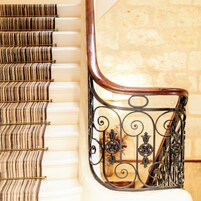 Escada com corrimão de madeira e guarda-corpo metálico com detalhes decorativos.