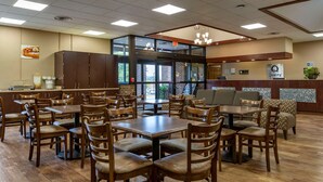 Um restaurante espaçoso com várias mesas e cadeiras de madeira, uma área de cozinha e um letreiro com a palavra 'Qualidade'.