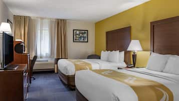 Quarto de hotel com duas camas, uma escrivaninha com televisão, uma luminária e um quadro na parede.