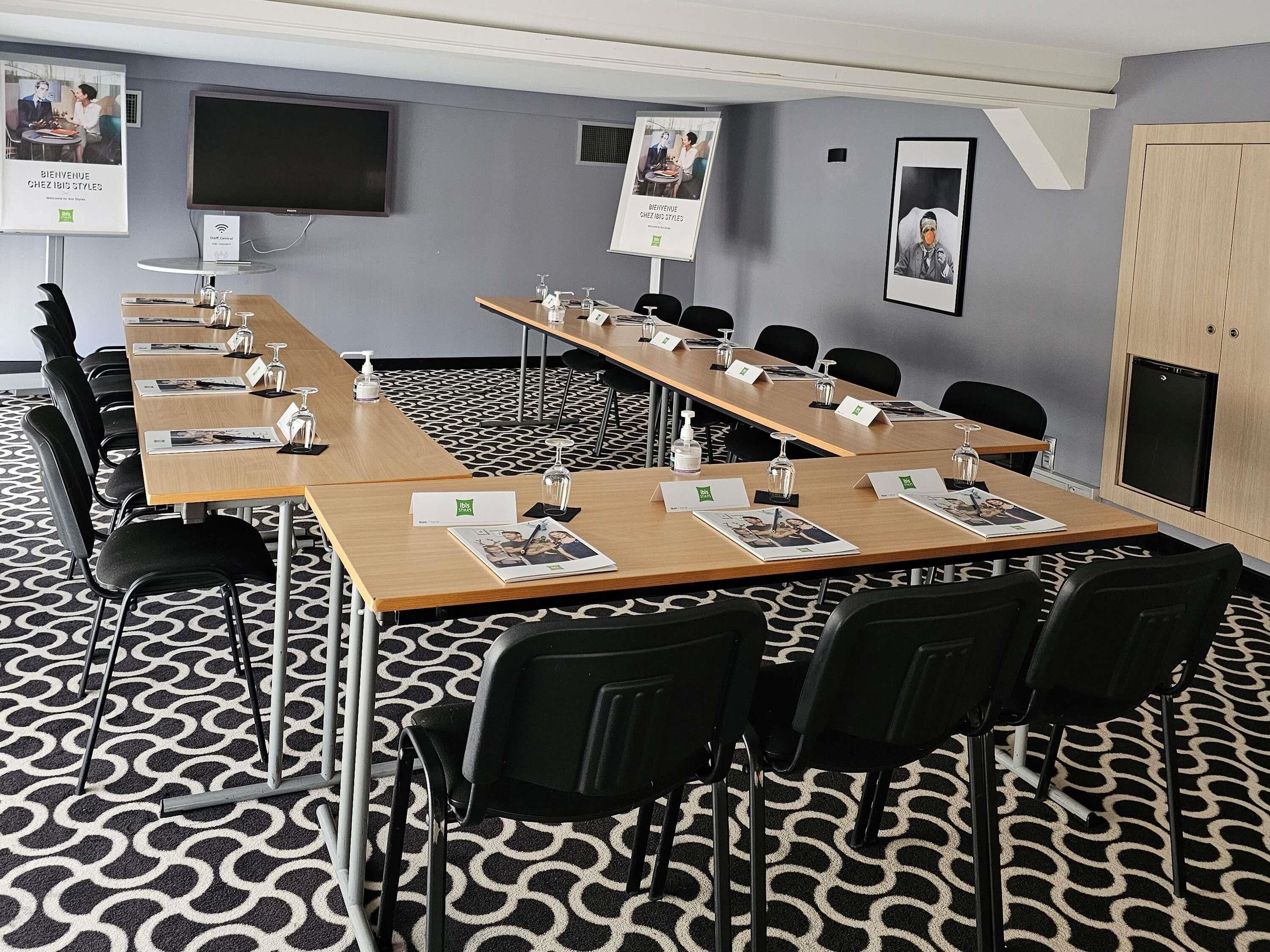 Uma sala de conferências com mesas compridas, cadeiras, cartões de nome e cartazes informativos.