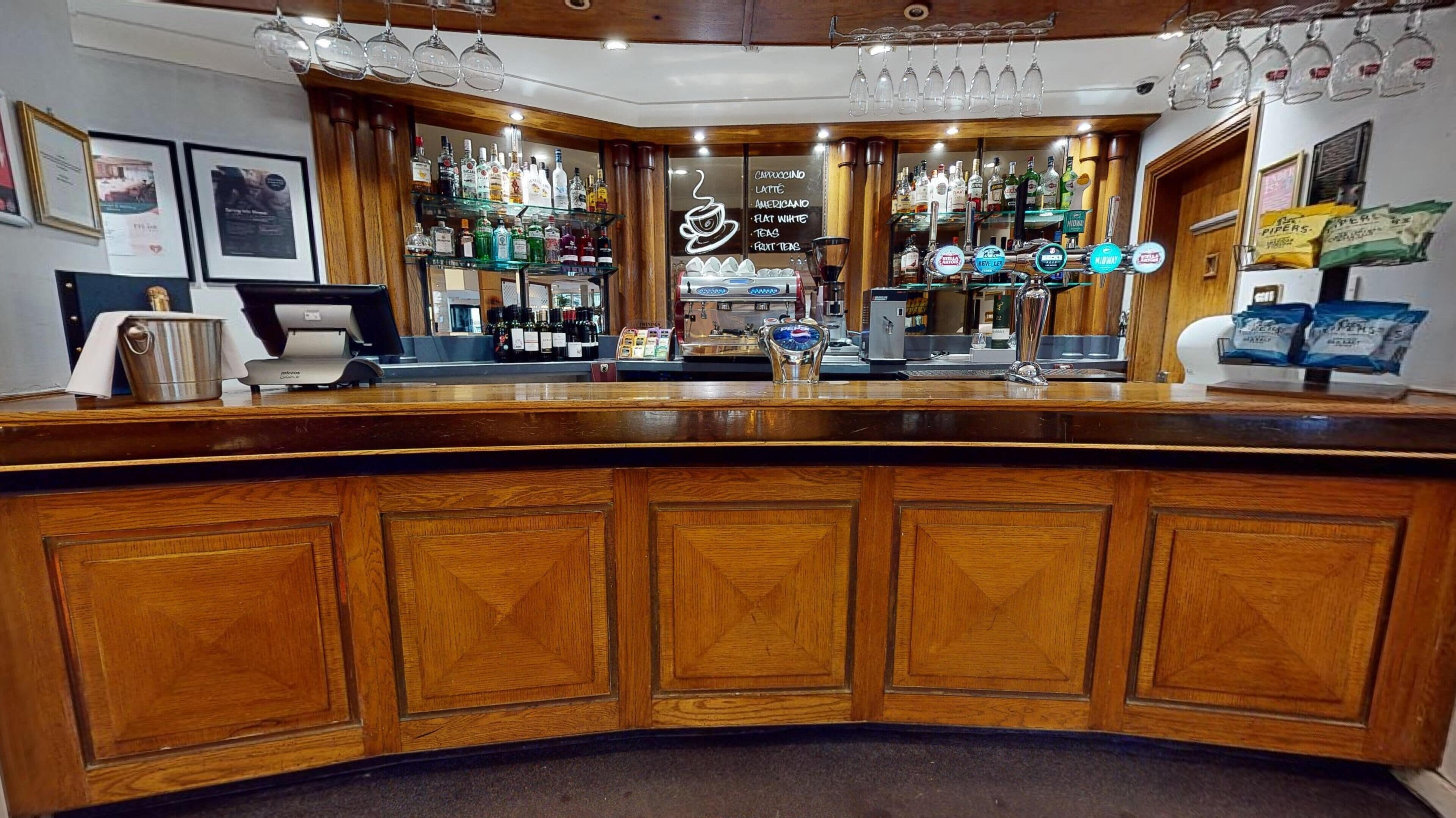 Uma área de bar com balcão, banquetas e uma seleção de garrafas de bebidas.