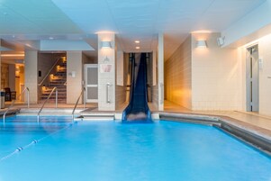 Piscina interior com escorrega, escada e placa indicando que o escorrega está em funcionamento.