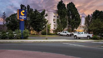 Um hotel Comfort Inn com uma placa chamativa, um estacionamento com caminhonetes brancas e ao fundo árvores e um céu nublado.