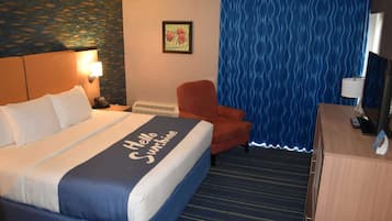 Quarto de hotel com cama, uma cadeira, escrivaninha, abajur e um quadro na parede.