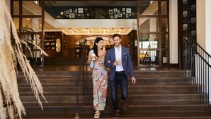 Um casal caminhando por uma escadaria de madeira no saguão de um hotel, com design de interiores moderno e vista para o andar superior.