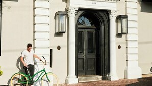 Um homem em pé ao lado de uma bicicleta verde em frente a um edifício com porta preta e colunas brancas.