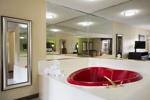 Uma casa de banho com uma banheira vermelha, um espelho grande e uma bancada branca.