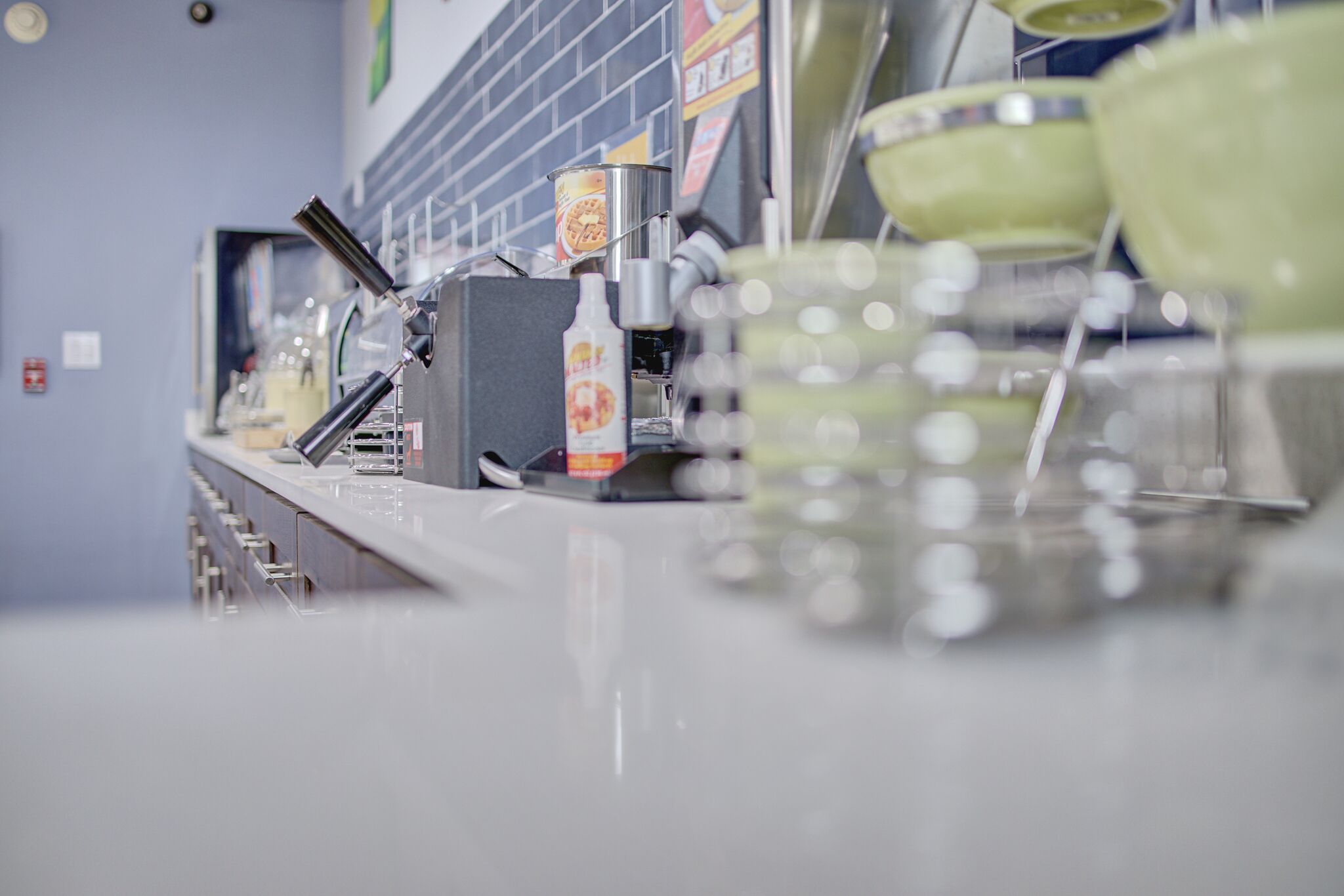 Máquina de café com vaporizador de leite e um recipiente, bancada com um copo, e parede com um letreiro.