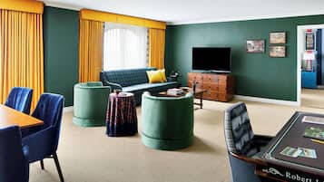 Uma sala de estar com um sofá verde, poltronas azuis, uma mesa de centro e uma televisão.