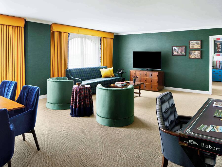 Uma sala de estar com um sofá verde, poltronas azuis, uma mesa de centro e uma televisão.