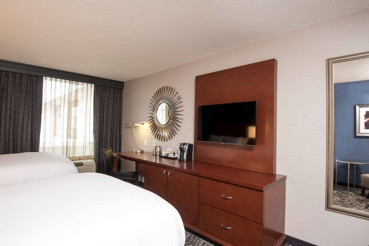 Quarto de hotel com uma cama grande, cômoda de madeira, televisão e espelho.