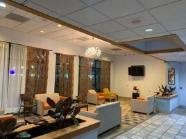 Um hall de hotel com um candelabro, área de estar e uma televisão fixada na parede.