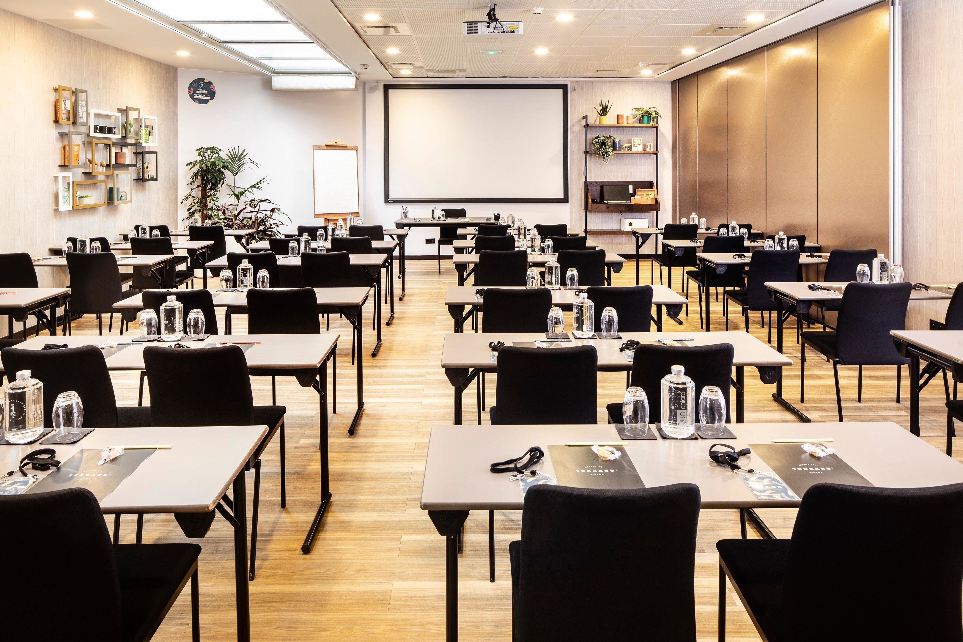 Sala de conferência com várias mesas e cadeiras, equipada com garrafas de água e cadernos.