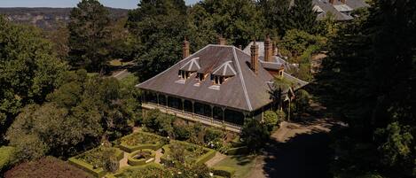 Uma grande propriedade com um gazebo imponente, jardins bem cuidados e diversas árvores.