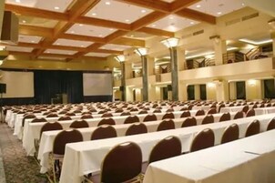 Uma sala de conferências com mesas e cadeiras dispostas em fileiras, um palco e uma varanda.