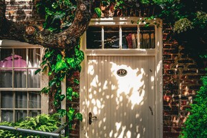 Uma porta de madeira branca com o número 19, uma janela com cortinas e hera crescendo na parede.