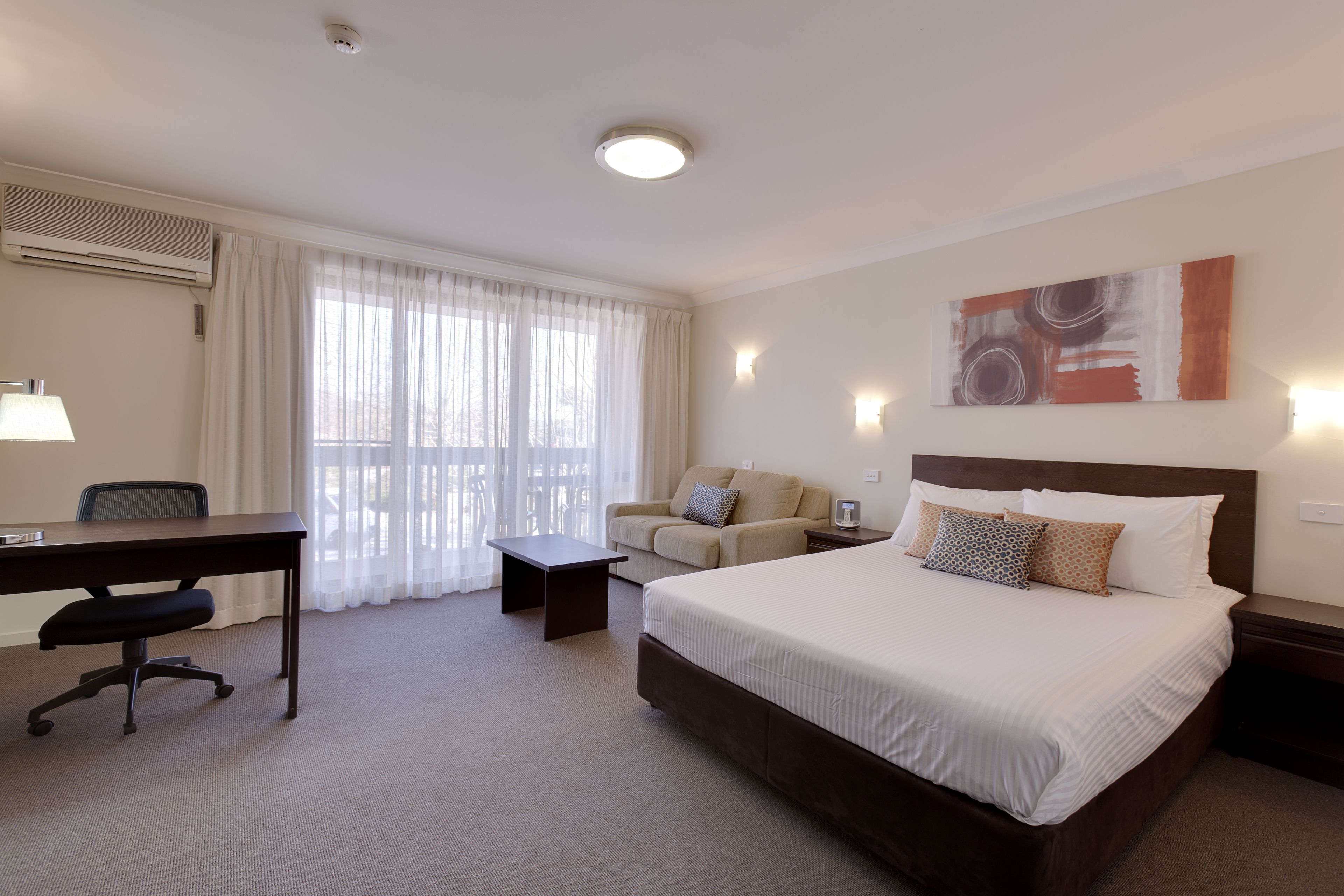 Quarto de hotel com cama, secretária, cadeira, sofá e um quadro na parede.
