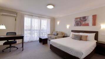 Quarto de hotel com cama, secretária, cadeira, sofá e um quadro na parede.
