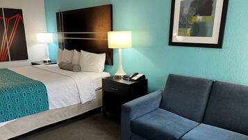 Quarto de hotel com uma cama, duas mesas de cabeceira, um sofá azul, uma pintura abstrata emoldurada e uma parede com padrão geométrico.