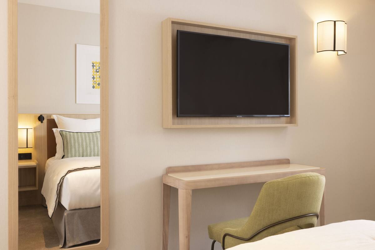 Quarto de hotel com uma cama, escrivaninha, cadeira, televisão de tela plana na parede e abajur.