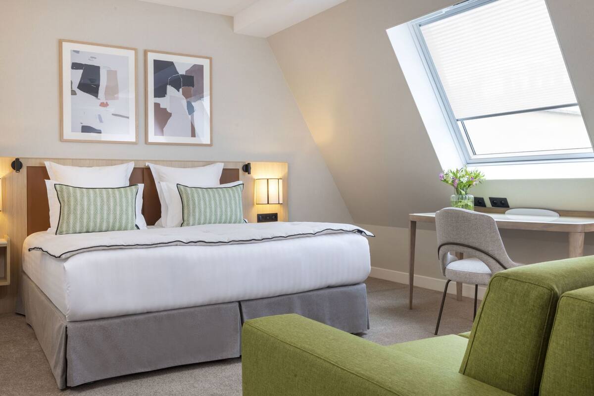 Quarto de hotel com cama, escrivaninha, cadeira e duas obras de arte emolduradas na parede.