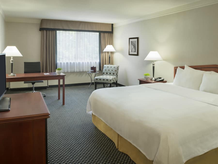 Quarto de hotel com uma cama grande, duas mesas de cabeceira, uma escrivaninha, uma cadeira e duas luminárias.