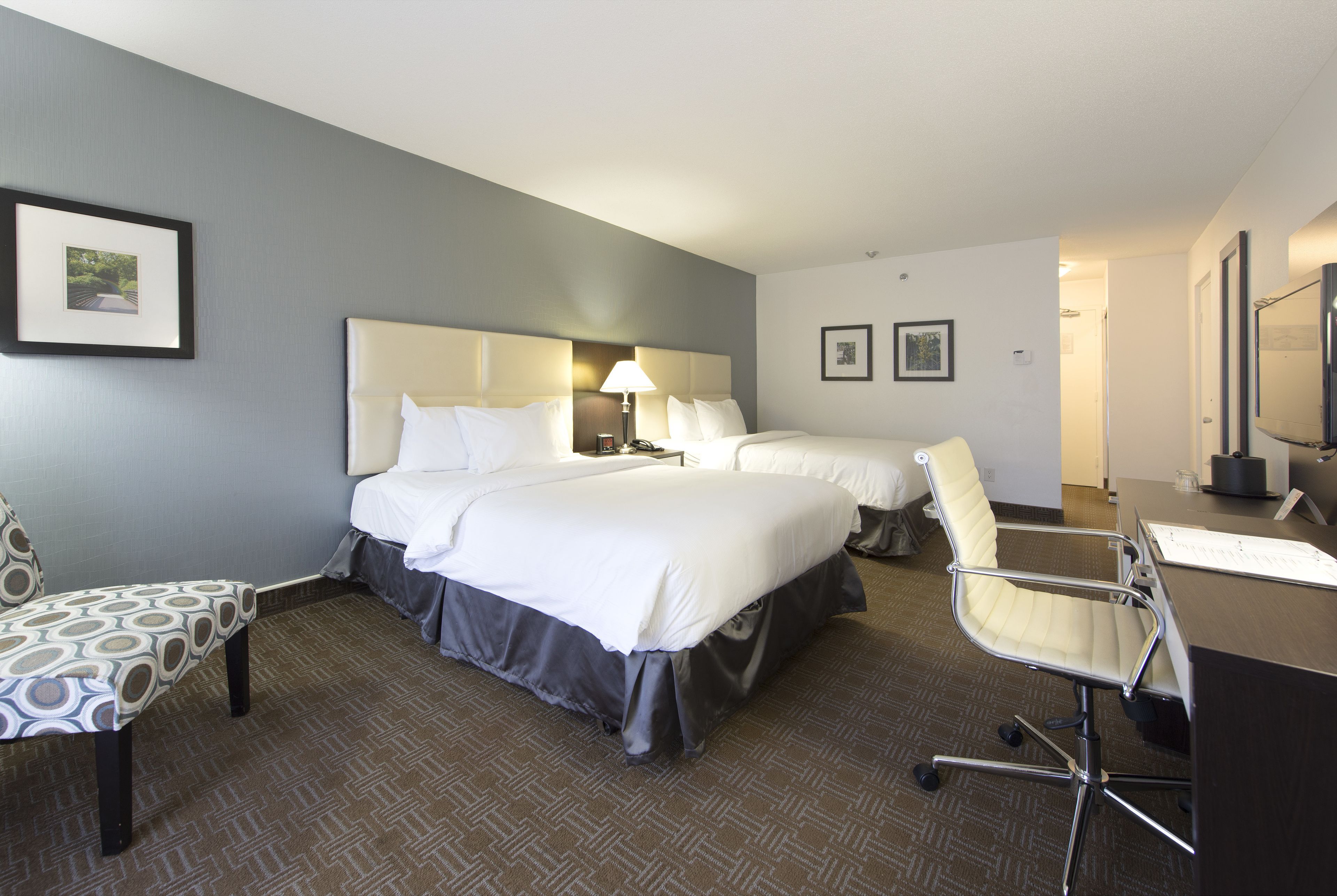 Quarto de hotel com duas camas, uma escrivaninha, uma cadeira e um espelho.