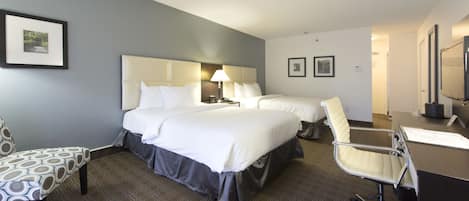 Quarto de hotel com duas camas, uma escrivaninha, uma cadeira e um espelho.