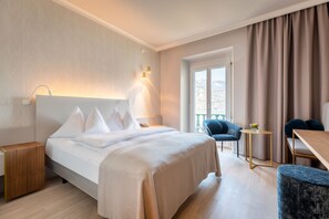 Quarto de hotel com cama, mesa de cabeceira, luminária, cadeira e vista para o exterior.