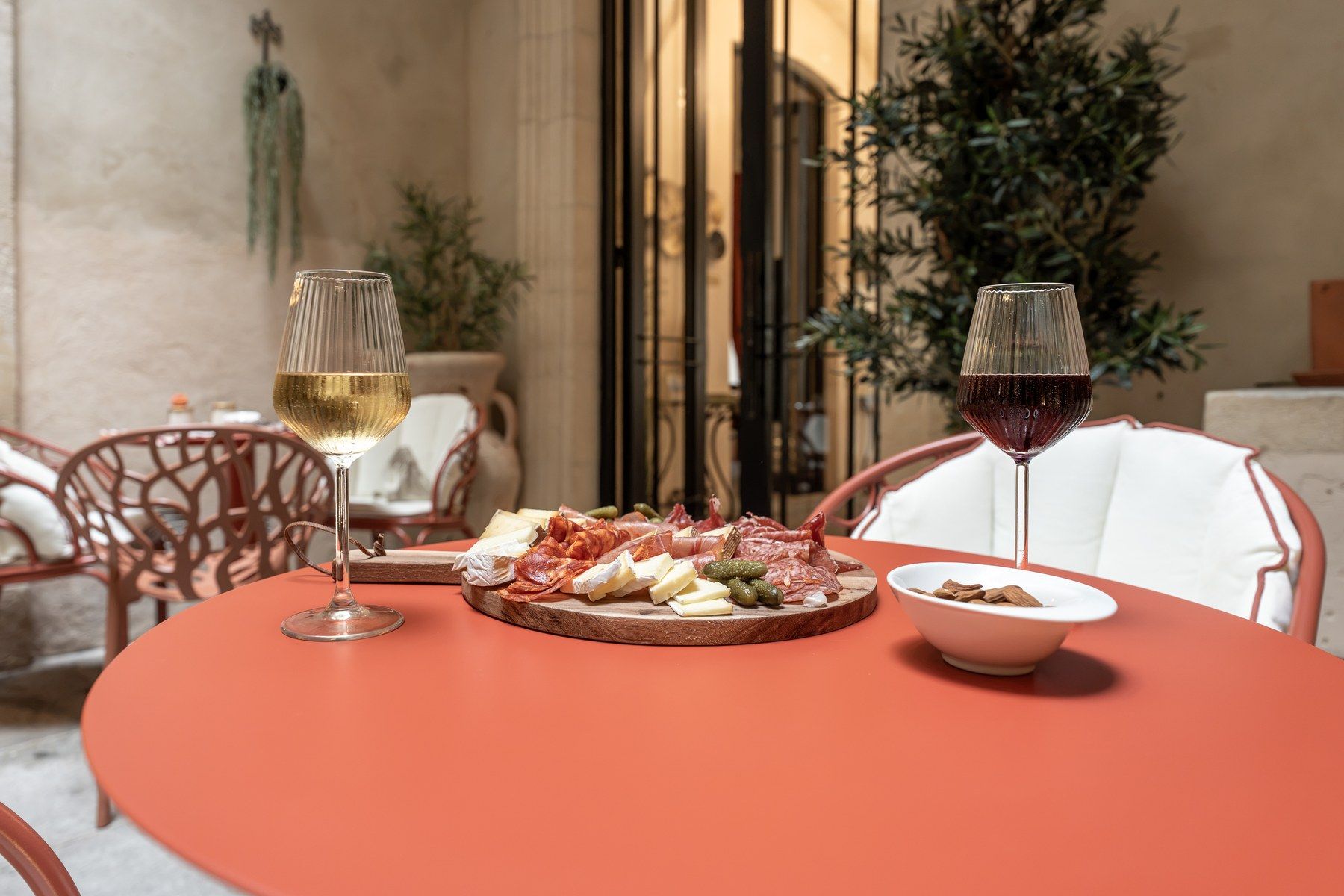 Uma mesa com uma tábua de frios, dois copos de vinho e uma tigela de nozes.