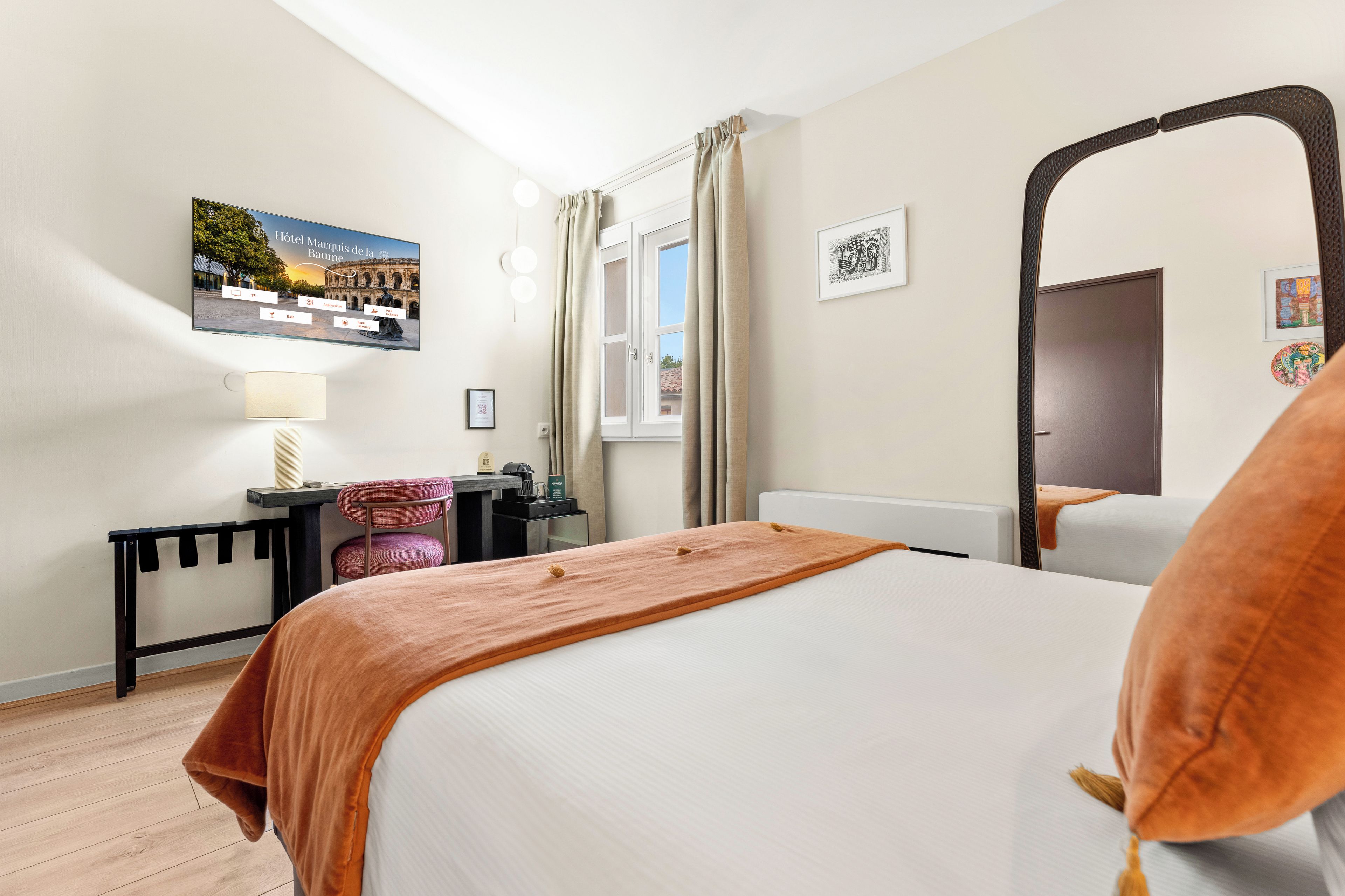 Quarto de hotel com cama, escrivaninha, cadeira, televisão e janela com cortinas.