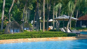Uma área de piscina com espreguiçadeiras, guarda-sóis e uma pequena construção semelhante a uma cabana.