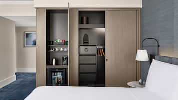 Quarto de hotel com cama, escrivaninha, minibar e guarda-roupa.