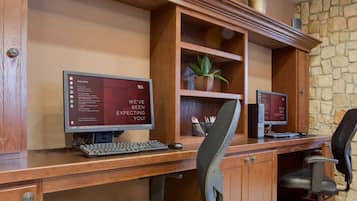Uma mesa de madeira com dois monitores, um teclado e duas cadeiras de escritório.