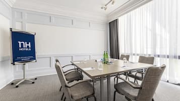 Uma sala de conferências com uma mesa grande, quatro cadeiras, uma tela de projetor e uma janela com cortinas.