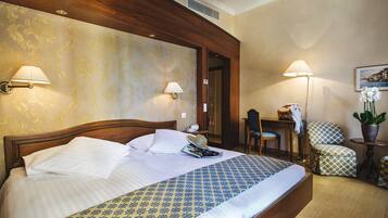 Quarto de hotel com uma cama grande, duas luminárias de cabeceira, uma escrivaninha com cadeira e um vaso de planta.