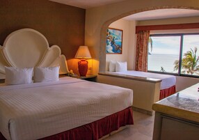 Quarto de hotel com duas camas, uma escrivaninha, uma luminária e um quadro.