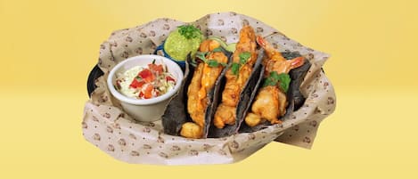 Cesta com três tacos de peixe, um recipiente de salsa e um recipiente de guacamole.