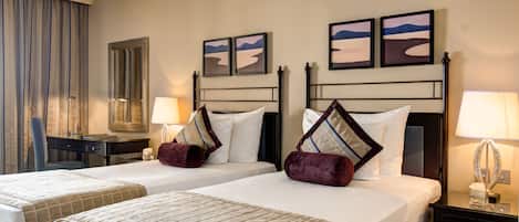 Quarto de hotel com duas camas, uma mesa de escritório e uma cadeira. Há duas mesas de cabeceira com abajures.