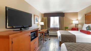 Quarto de hotel com cama, escrivaninha, televisão e ar condicionado.