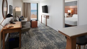 Quarto de hotel com cama, escrivaninha, cadeira, televisão, espelho e vista para a praia.
