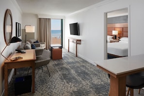 Quarto de hotel com cama, escrivaninha, cadeira, televisão, espelho e vista para a praia.