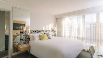 Quarto de hotel com uma cama grande, uma escrivaninha, uma cadeira, um espelho e uma janela com cortinas.