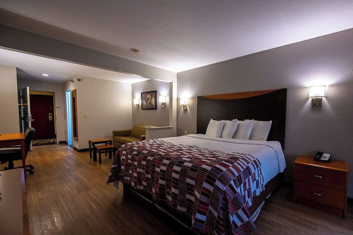 Quarto de hotel com uma cama grande, uma escrivaninha, uma cadeira e uma mesinha.