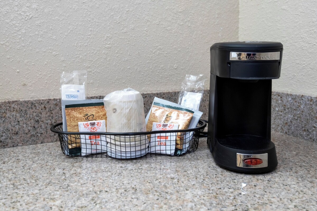 Máquina de café e cesta com saquinhos de chá e um rolo de papel toalha em uma bancada.