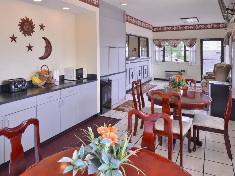 Quarto de hotel com cozinha, mesa de jantar e cadeiras. Apresenta detalhes decorativos nas paredes e uma janela com cortinas.