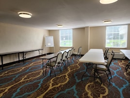 Sala de conferências com quadro branco, mesas, cadeiras e carpete estampado.